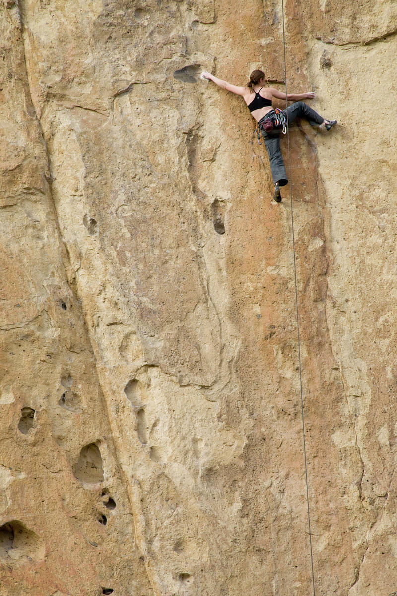 USA, Oregon, Smith Rock State Park. Woman climbs vertical rock cliff ...