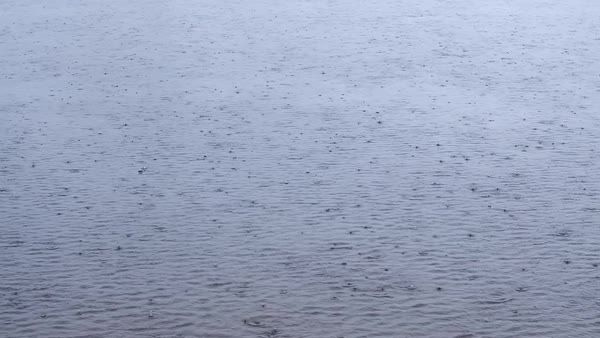 Drops of rain are falling into the blue water outdoors. Heavy rain on ...