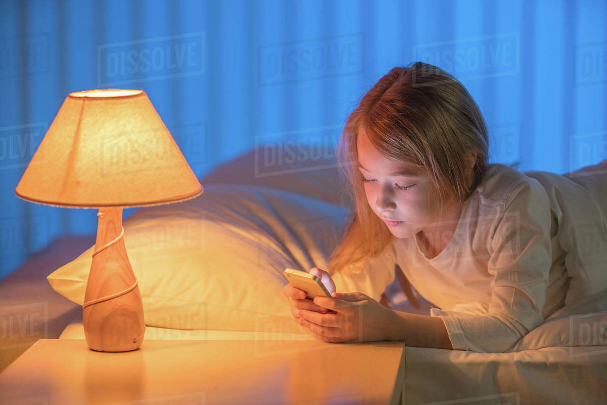 The girl with a phone lay on the bed. Evening night time - Stock Photo ...