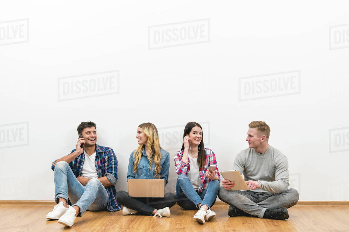 The four people with gadgets sit on the floor on the white wall ...