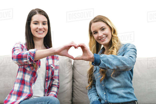 The two women show the heart symbol on the white wall background ...
