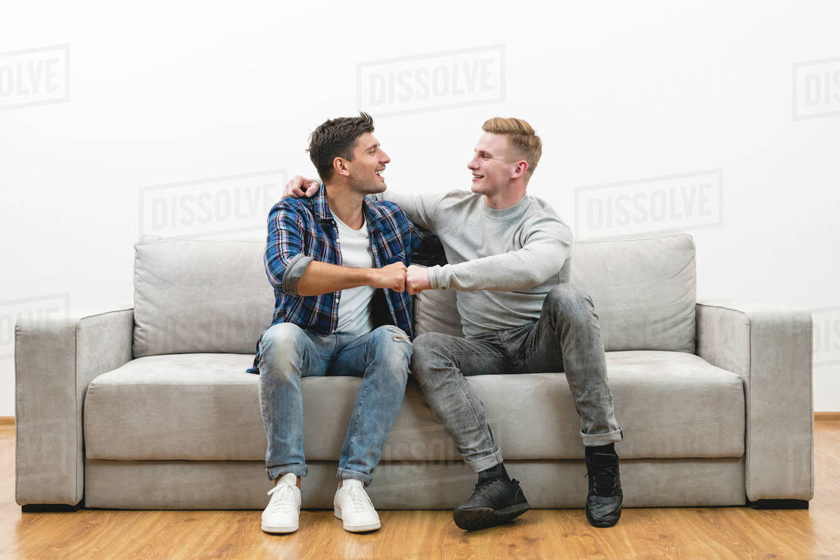 The two happy men on the sofa gesture on the white wall background ...