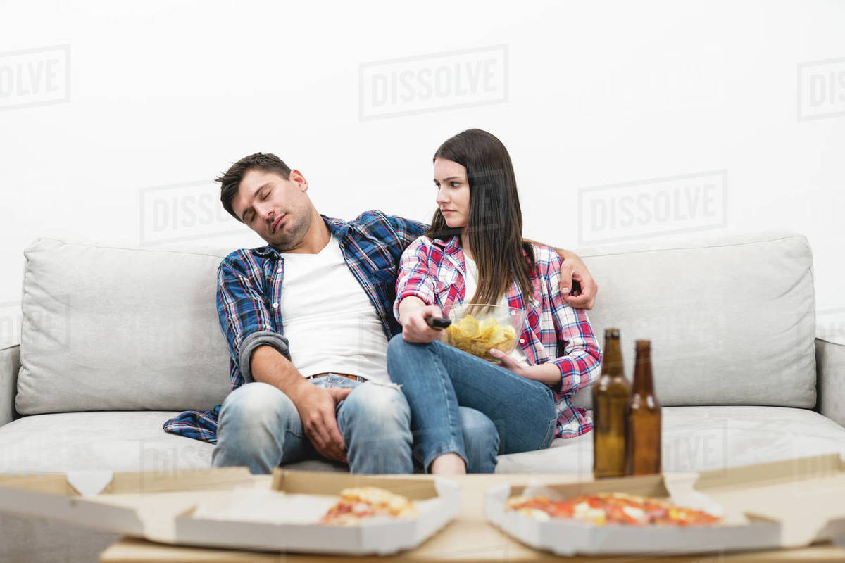 The sleeping man and a woman with chips sit on the sofa on the white ...