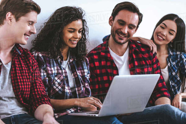 The happy four people with a laptop sitting on the floor - Royalty-free ...