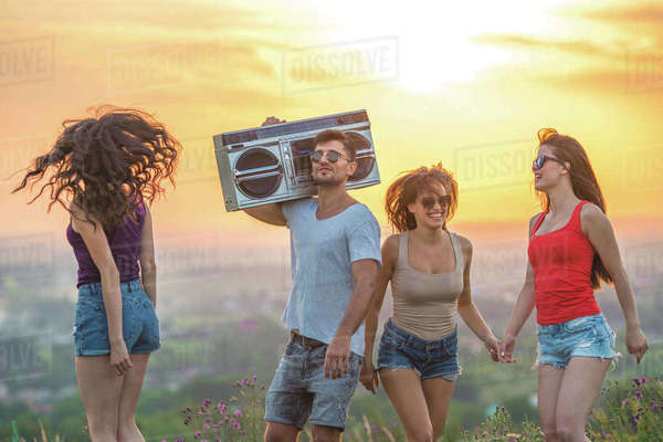 The four people dancing with a boom box on the sunset background ...