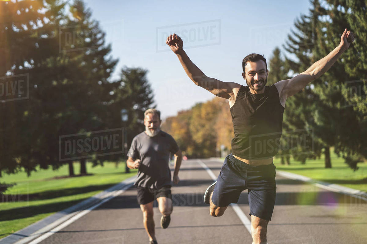 The two men running on the road in the park on the sunny background ...