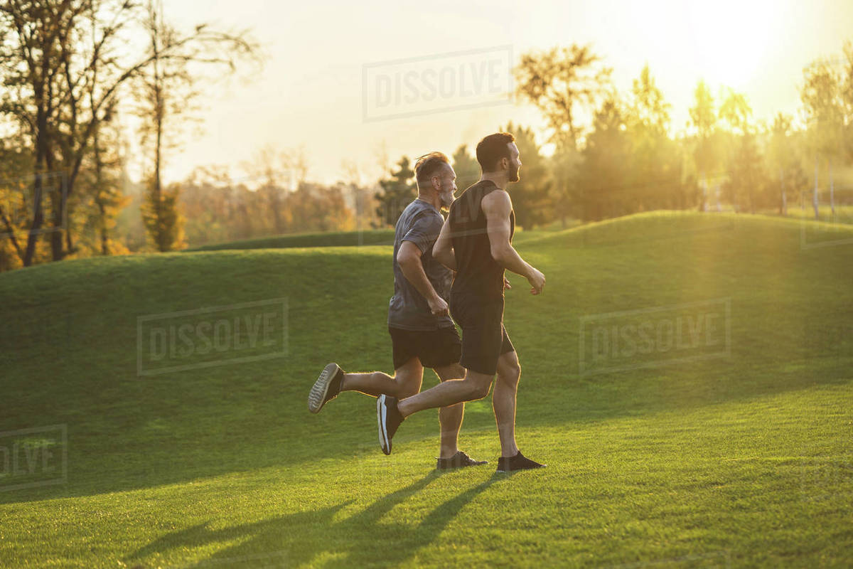 The two men running on the grass in the park on the sunrise background ...