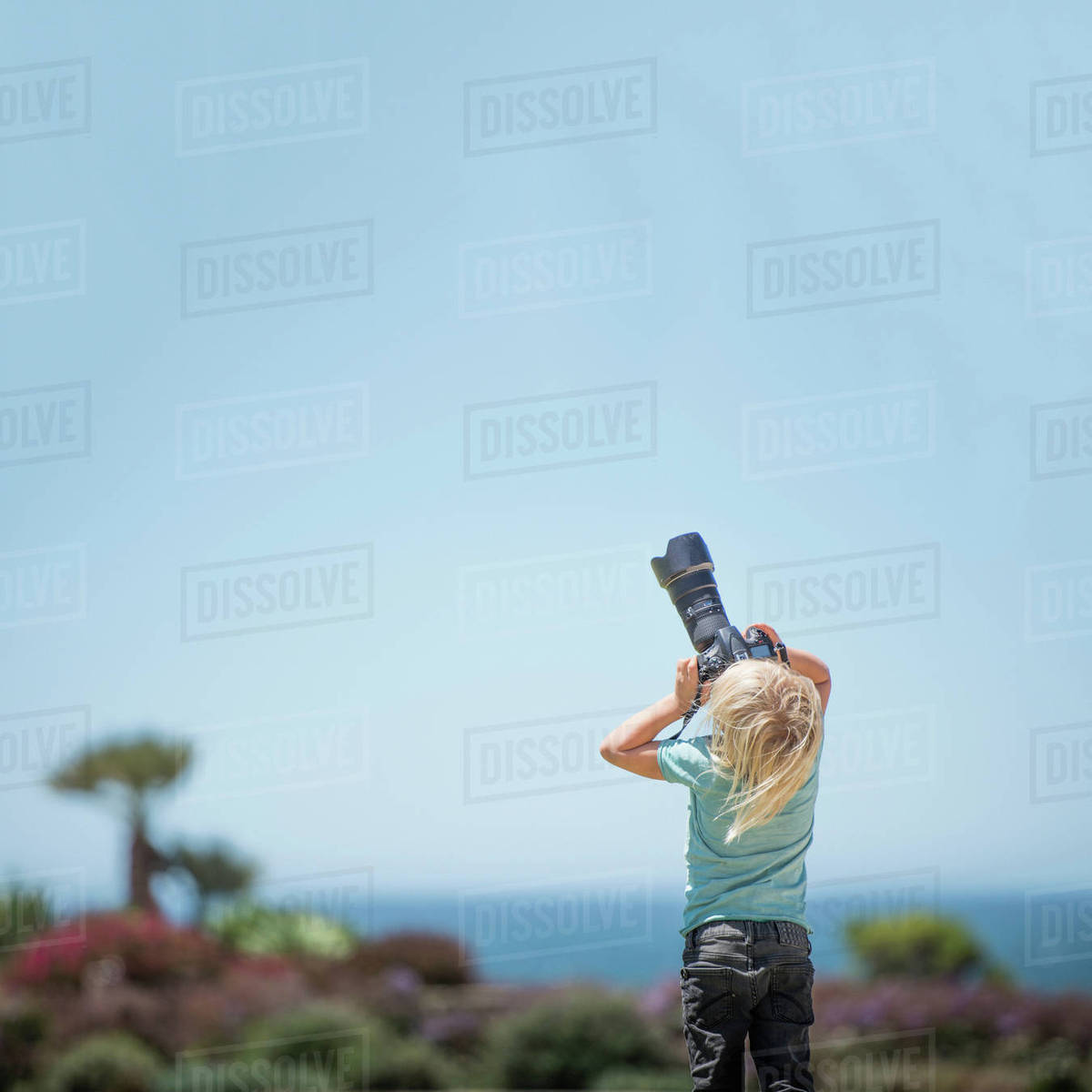 Rear view of boy looking up taking photograph with digital camera ...