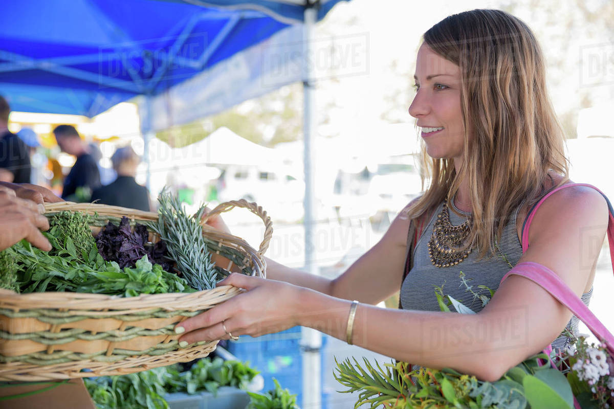 Woman at fruit and vegetable stall receiving basket of fresh herbs ...