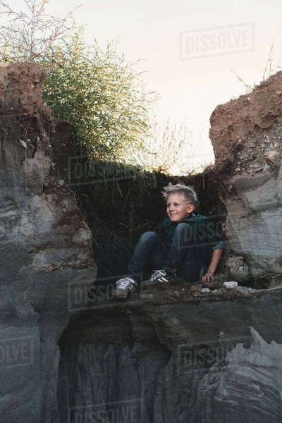 Boy hiding on ledge below cliff edge - Royalty-free Stock Photo | Dissolve