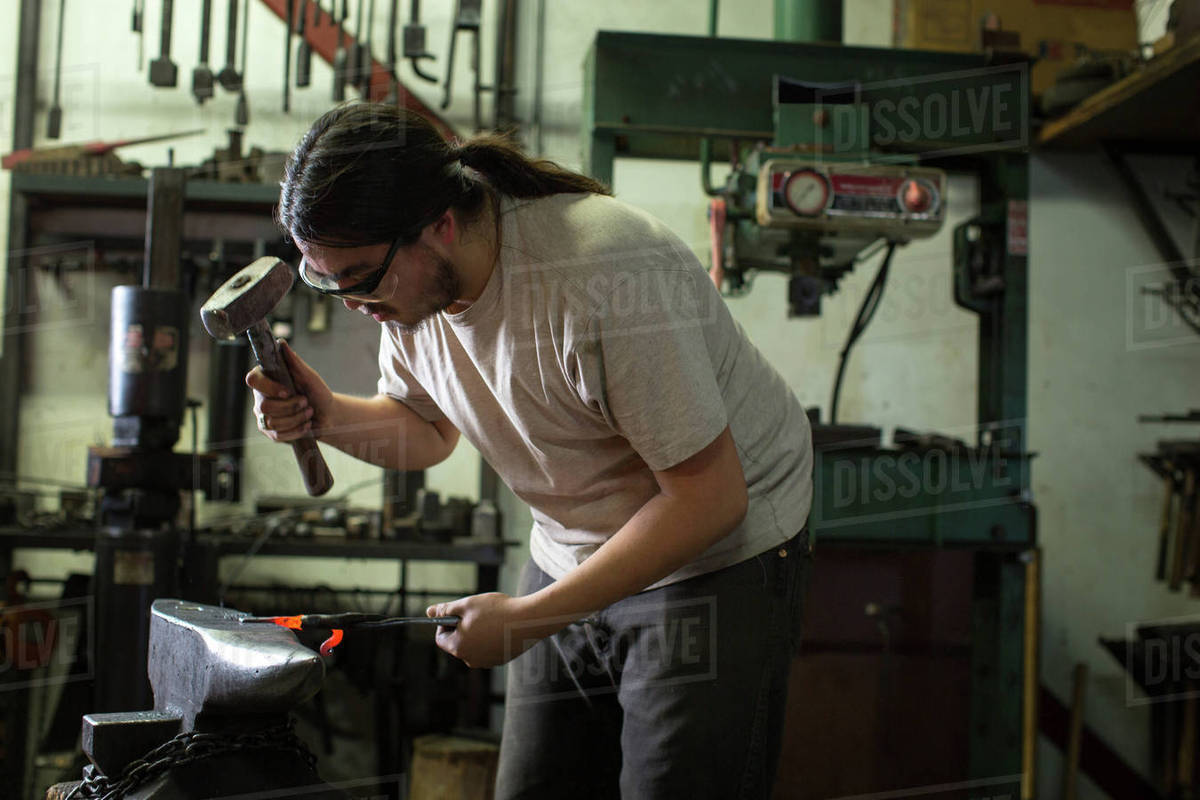 Male metalsmith hammering red hot metal on workshop anvil - Royalty ...