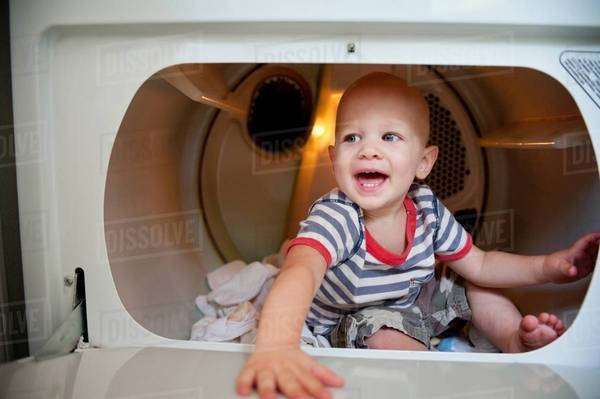 Baby boy sitting in tumble dryer - Stock Photo - Dissolve