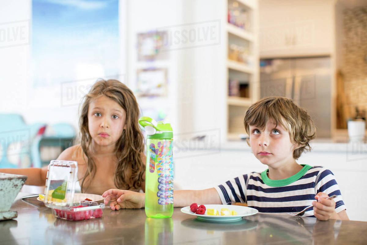 Boy and girl at kitchen table pulling faces - Royalty-free Stock Photo ...
