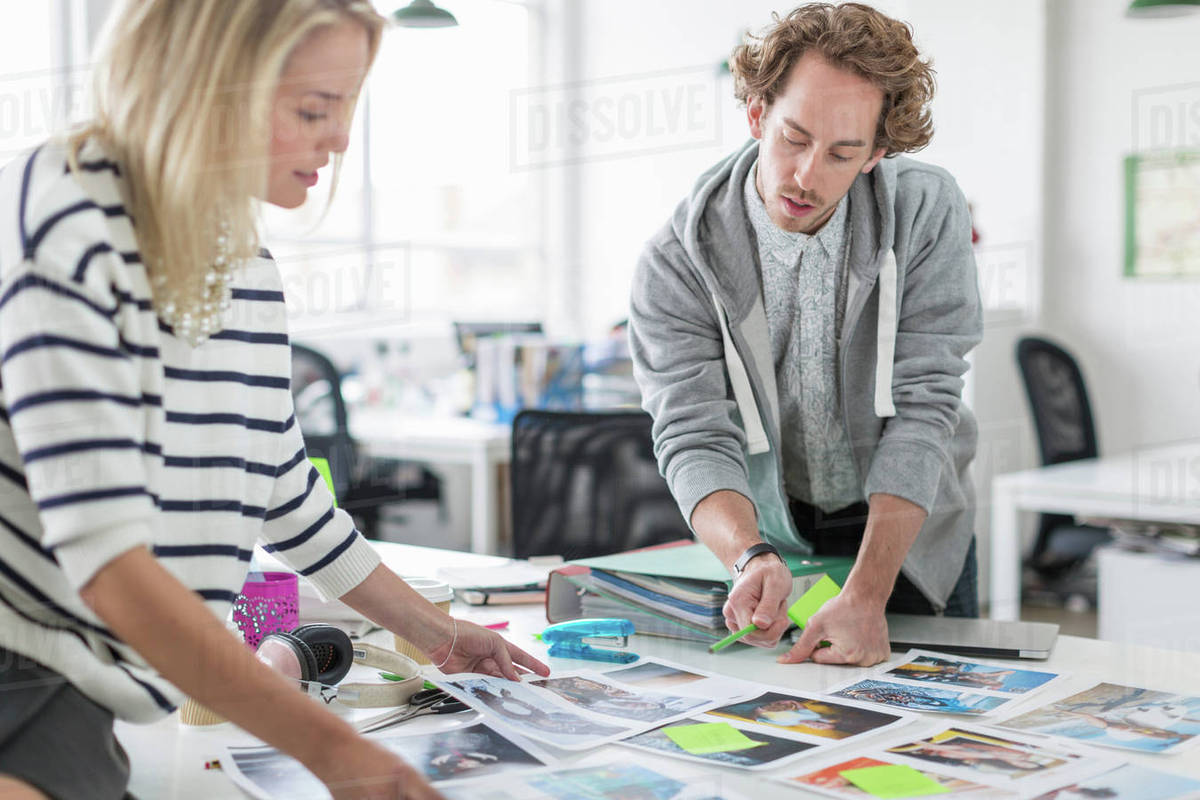 Young colleagues discussing photographs in meeting in creative office ...