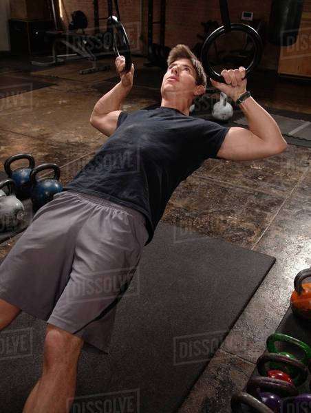 Bodybuilder on floor in gym using rings - Stock Photo - Dissolve