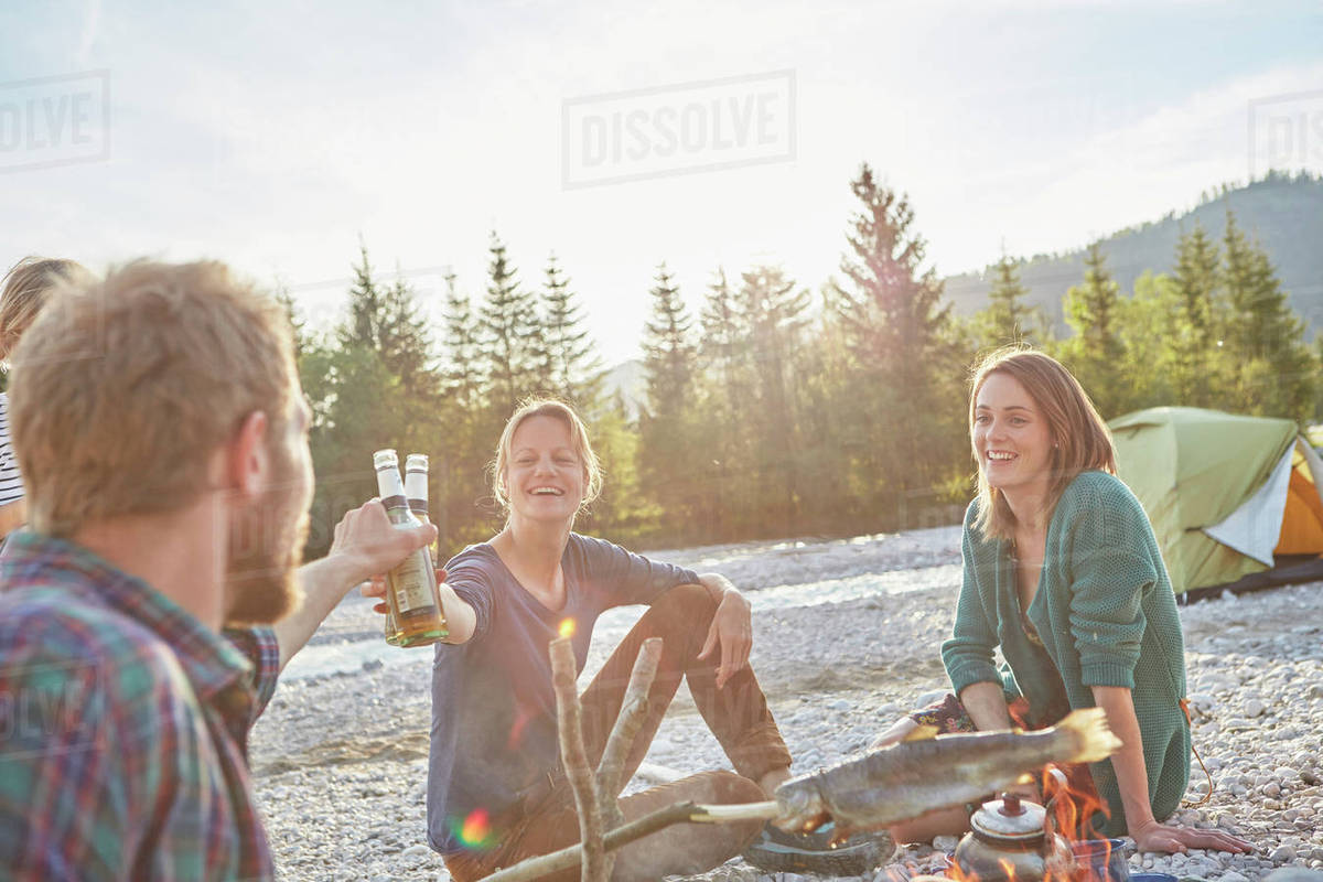 Adults sitting around campfire making a toast with beer bottles - Stock ...
