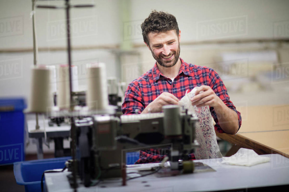 Male textile designer using sewing machine in old textile mill ...