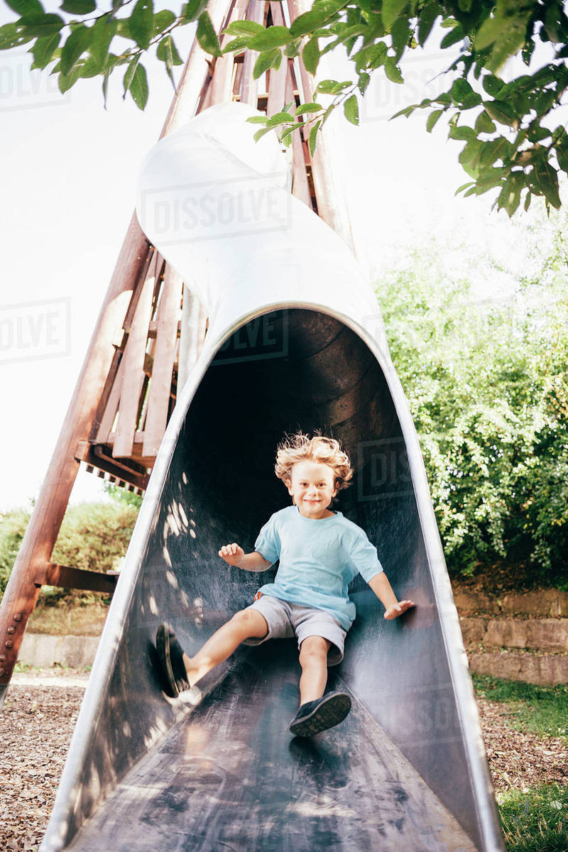 Boy sliding down playground slide looking at camera smiling, Ulm, Baden ...
