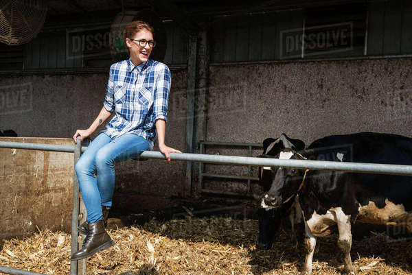 Female farmer sitting on fence at organic dairy farm - Royalty-free ...