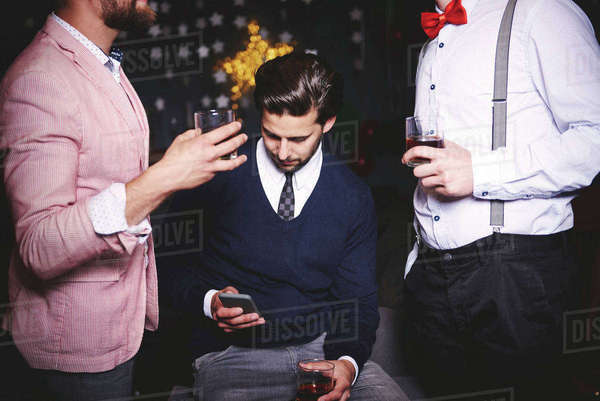 Three men at party, man in middle using smartphone - Royalty-free Stock ...