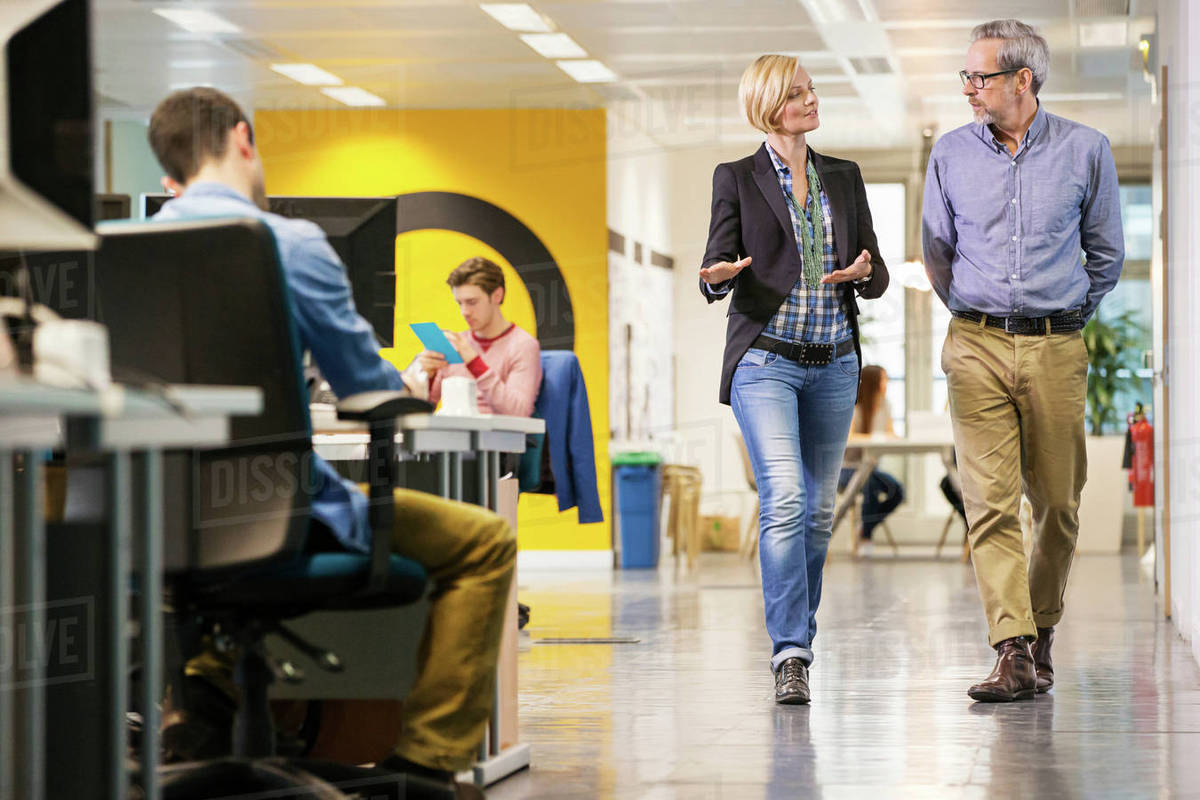 Female and male digital designers walking and talking in office ...