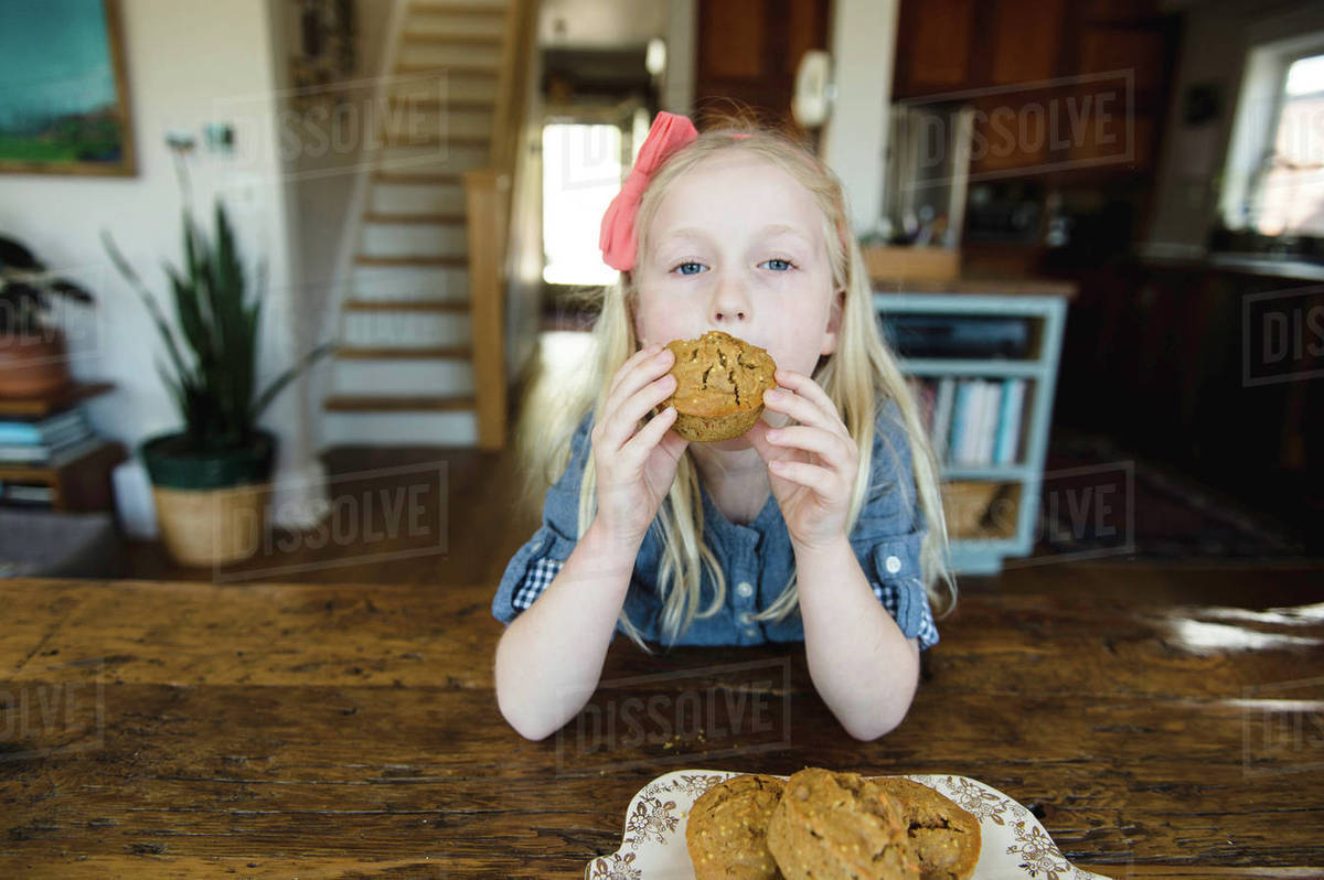 Portrait of girl eating muffin at kitchen table - Royalty-free Stock ...
