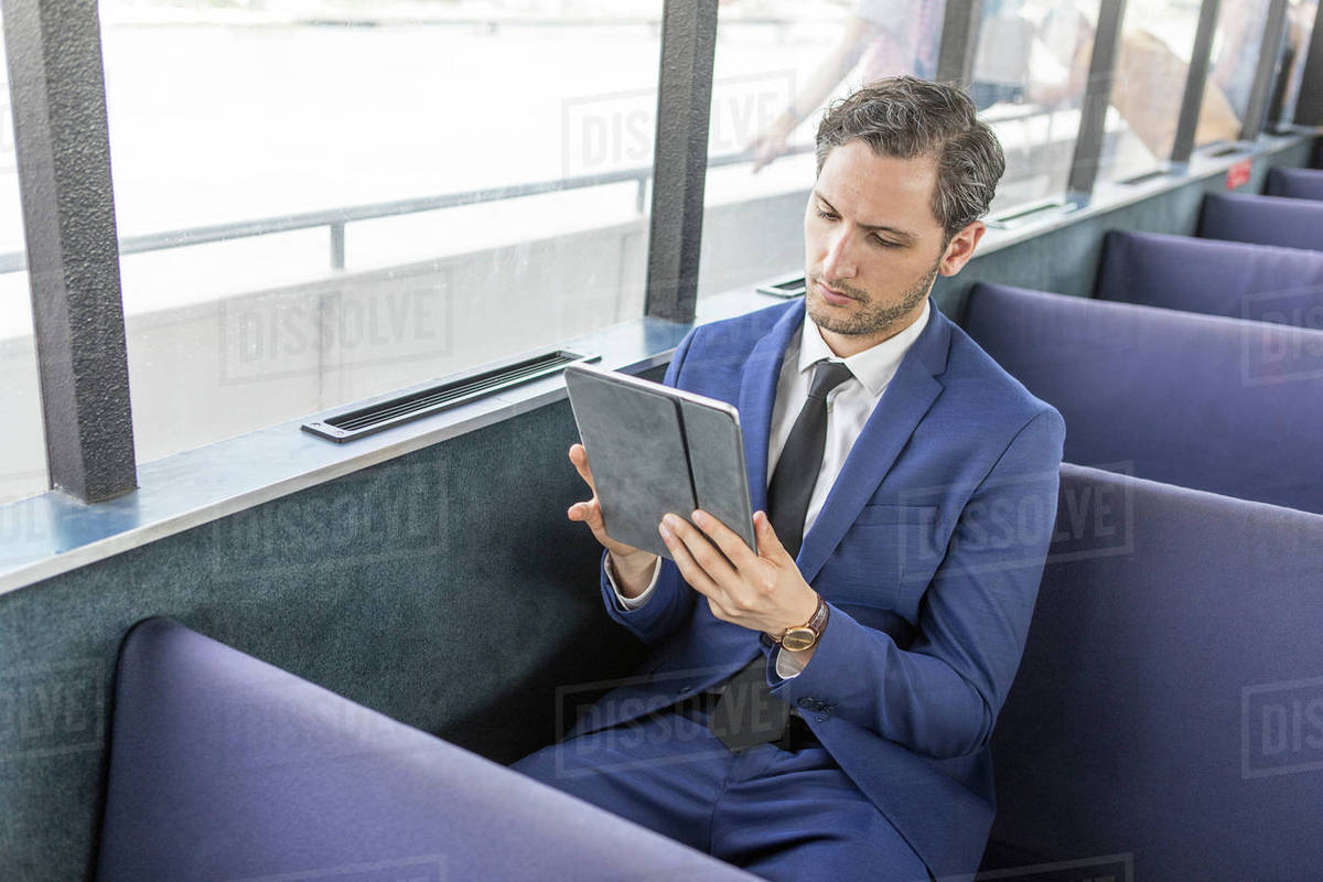 Young businessman on passenger ferry looking at digital tablet ...