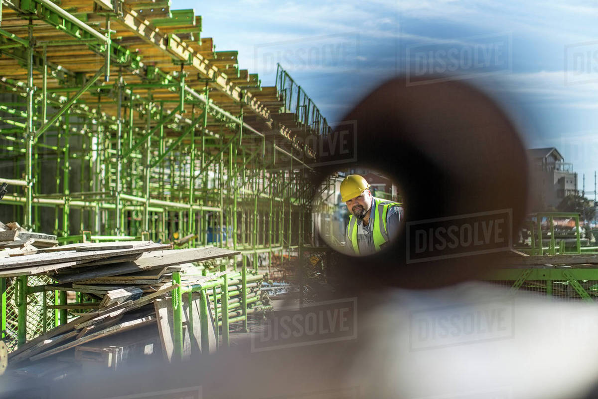Construction worker looking through pipe - Stock Photo - Dissolve