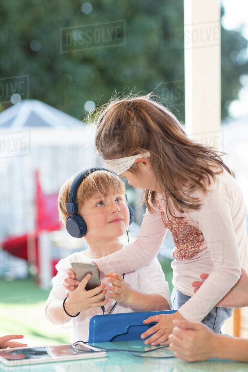 Two young children holding smartphone, young boy wearing headphones ...