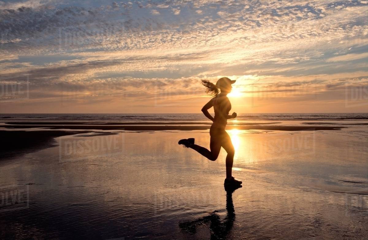 Woman running on beach at sunrise - Royalty-free Stock Photo | Dissolve