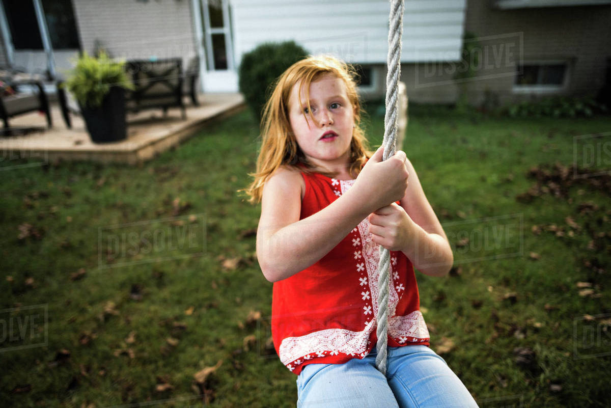 Girl swinging on rope in garden - Stock Photo - Dissolve