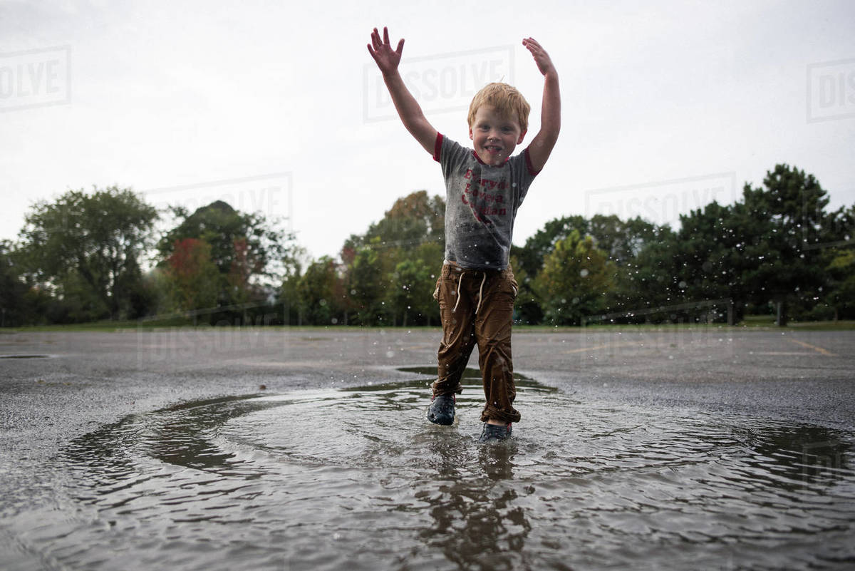 Boy playing in puddle on road - Royalty-free Stock Photo | Dissolve