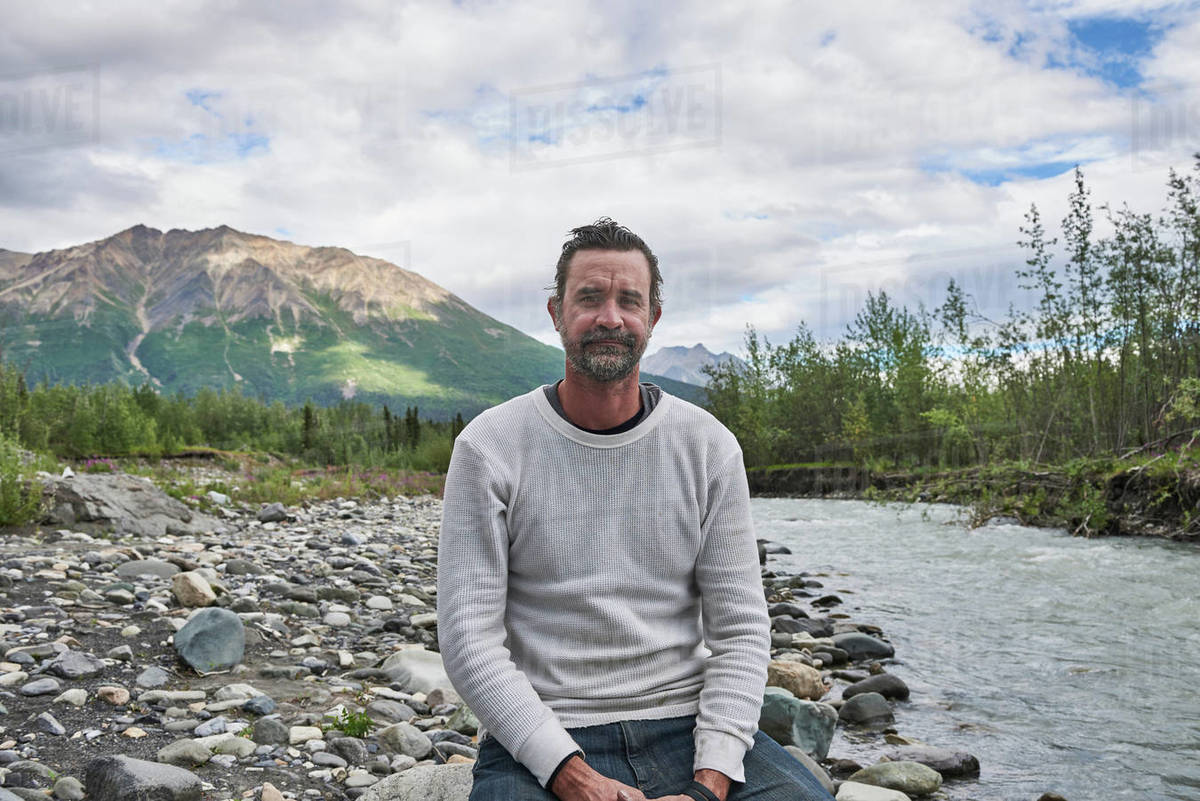 Man relaxing by stream, scenic view in background, Chitina, Alaska ...