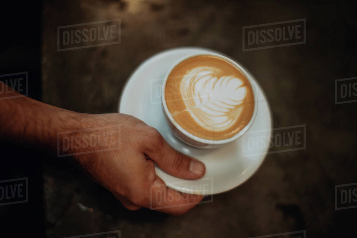 Barista placing cup of latte on cafe counter, overhead close up of hand ...