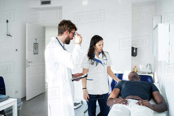 Doctor watching nurse examine patient in consultation room - Royalty ...