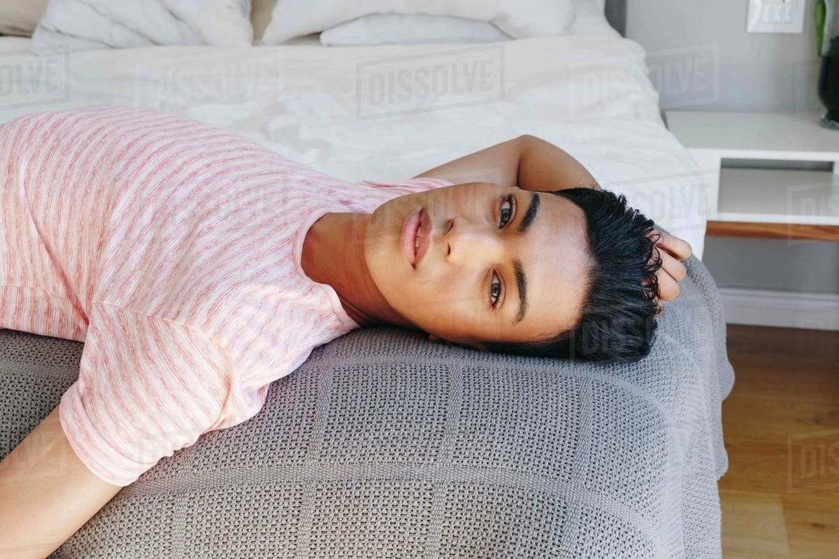 Young man lying back on bed, portrait - Stock Photo - Dissolve