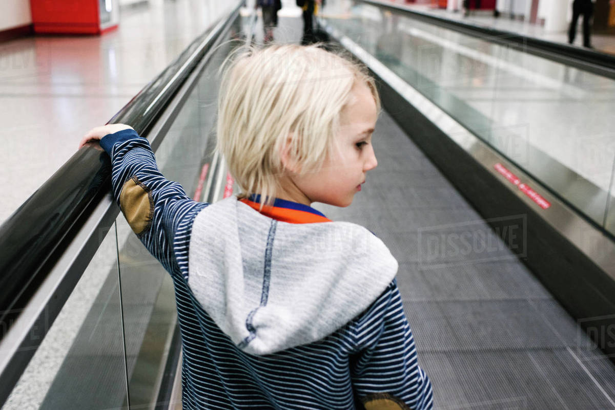 Blond haired boy on airport moving walkway looking over his shoulder ...