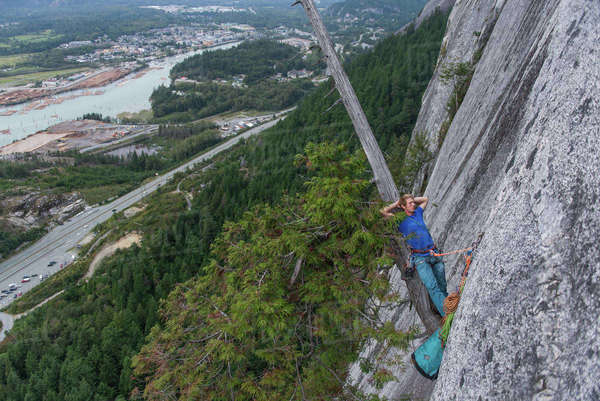Climber sleeping leaning back on a tree growing out of the cliff face ...