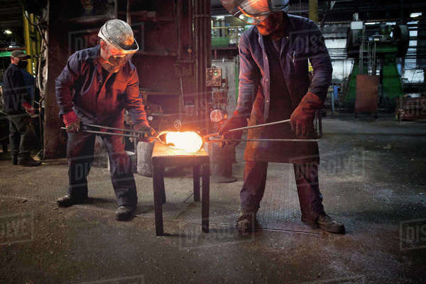 Forge worker hands over pre formed steel billet to colleague - Royalty ...