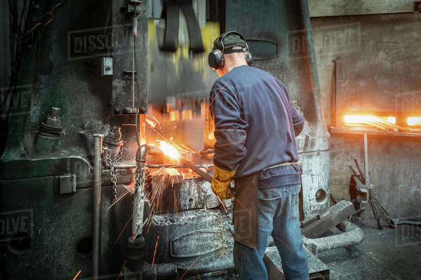 Rear view of engineer forging steel parts in hammer press in industrial ...