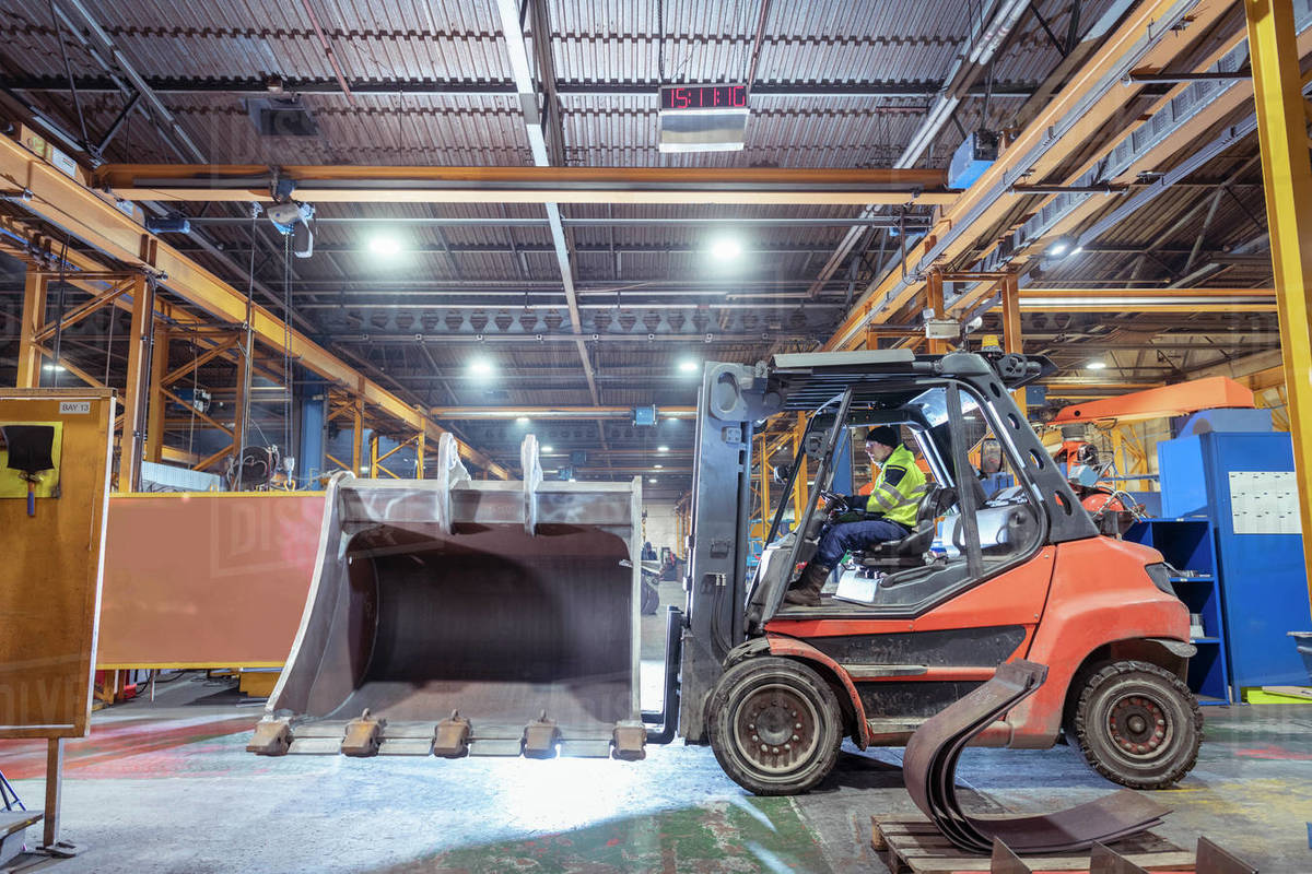 Man in forklift moving large digger bucket in engineering factory ...