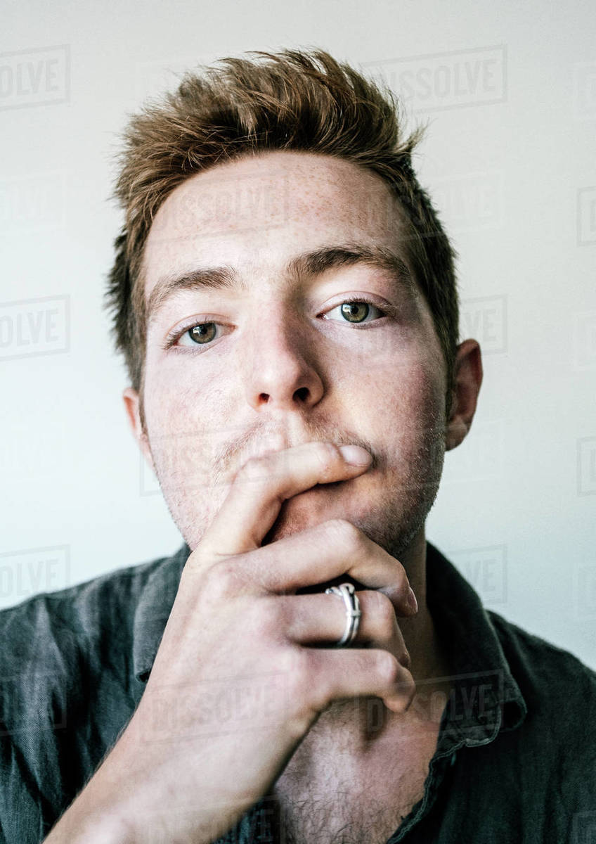 Studio portrait of young man covering mouth - Stock Photo - Dissolve