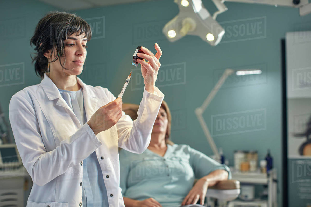Female doctor preparing botox injection, patient in background - Stock ...