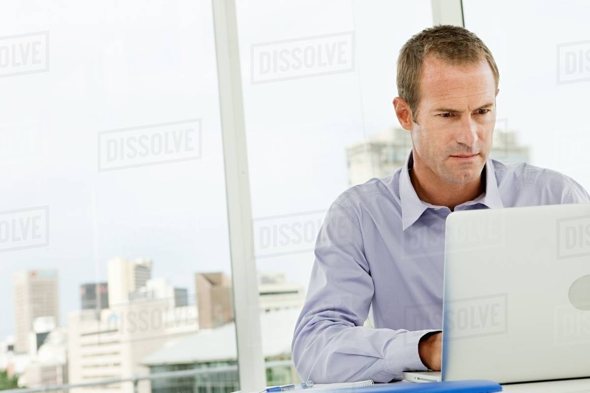 Businessman using laptop in office - Stock Photo - Dissolve