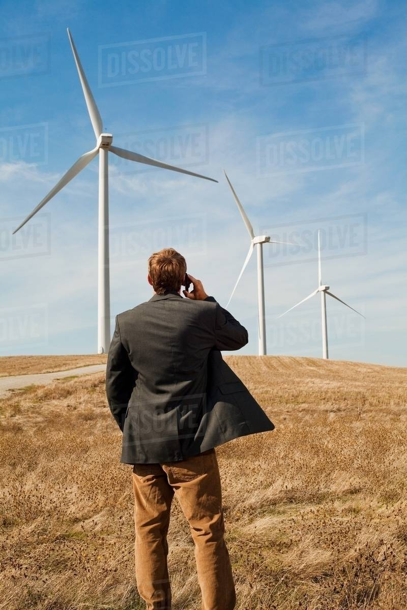 Man standing in front of wind turbines on mobile phone - Royalty-free ...