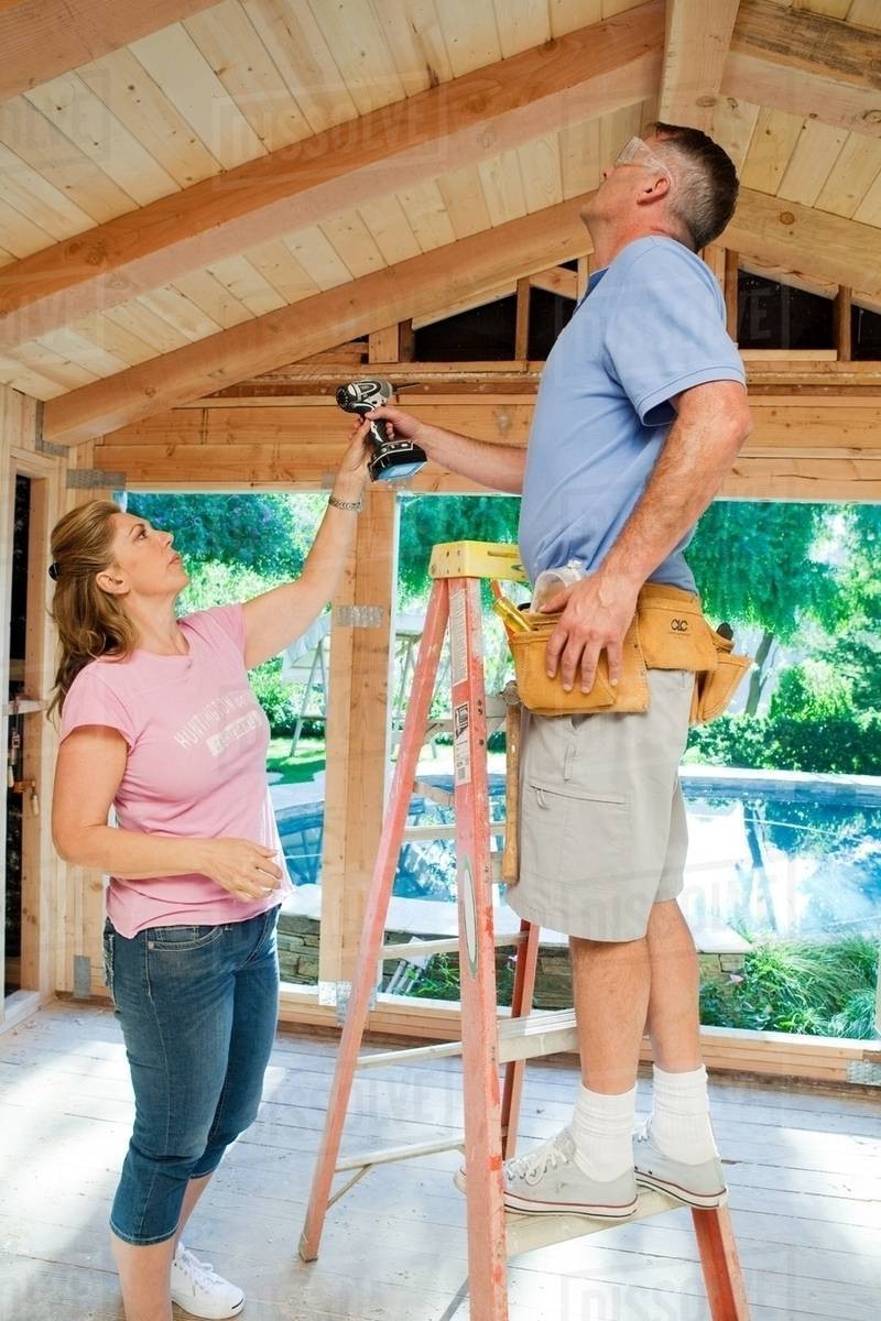 Mature woman passing tool to man on ladder - Royalty-free Stock Photo ...