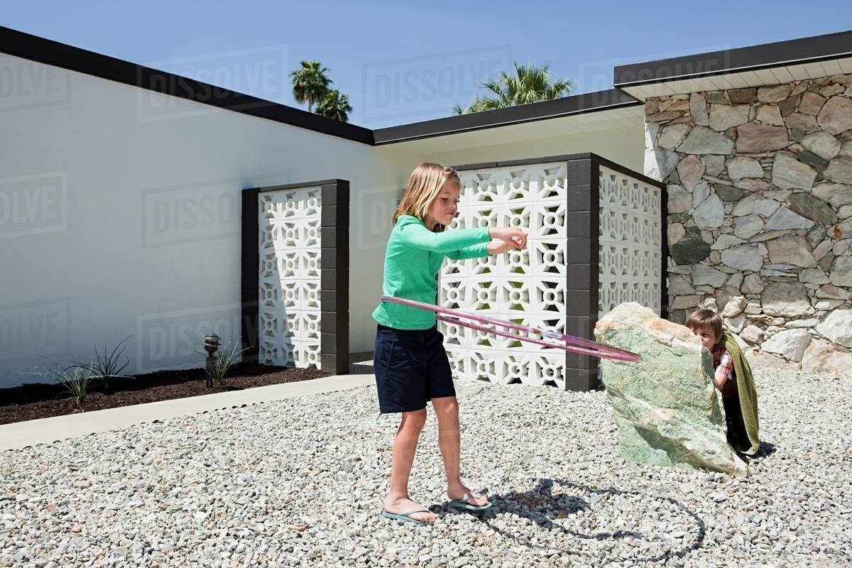 Brother hiding behind rock watching sister with hoola hoop - Royalty ...