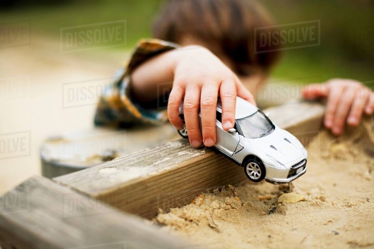 Male toddler holding toy car above sandpit - Royalty-free Stock Photo ...
