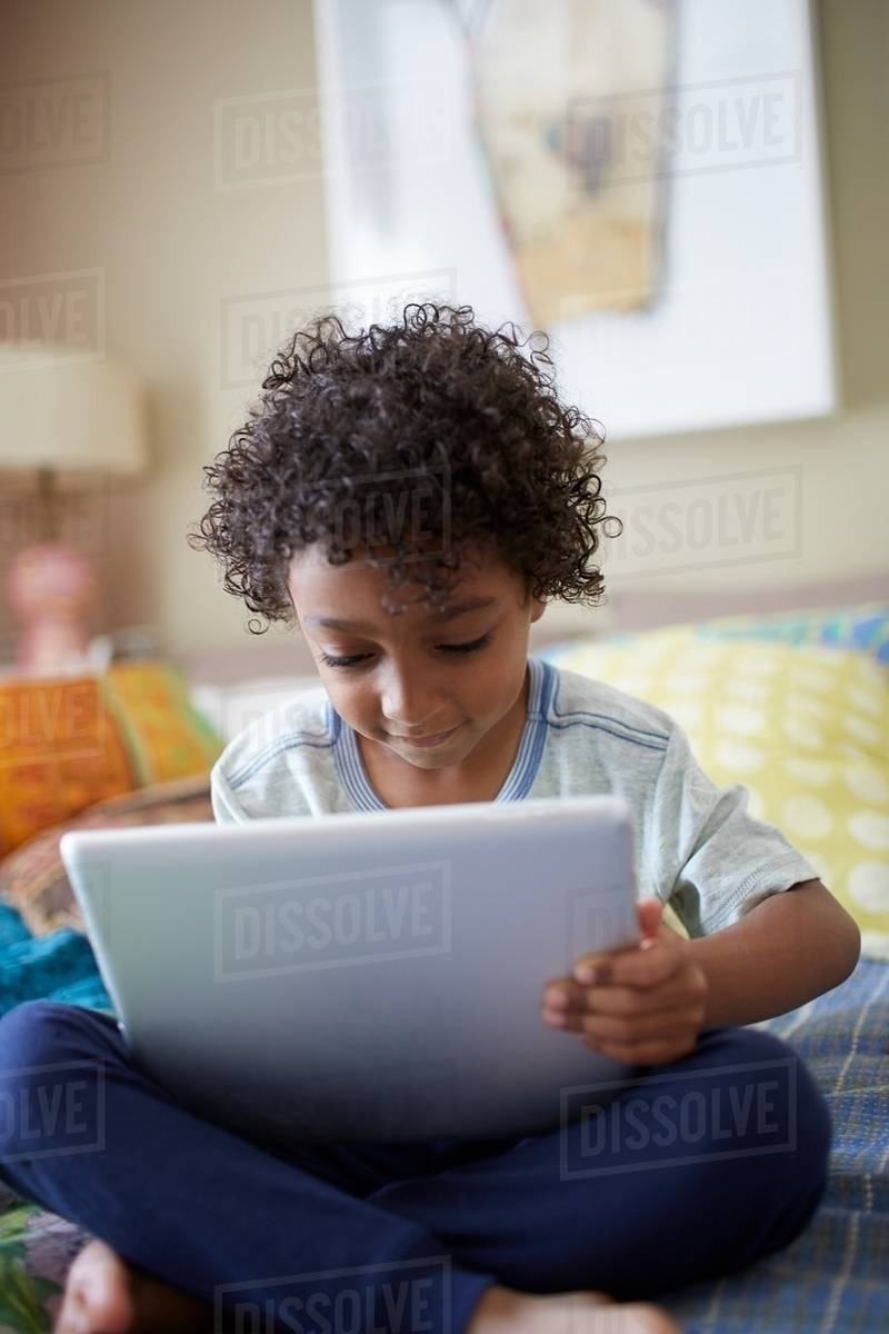 Child sitting on bed using digital tablet - Royalty-free Stock Photo ...