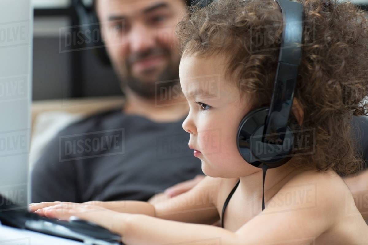 Close up of female toddler typing on laptop whilst father watches ...